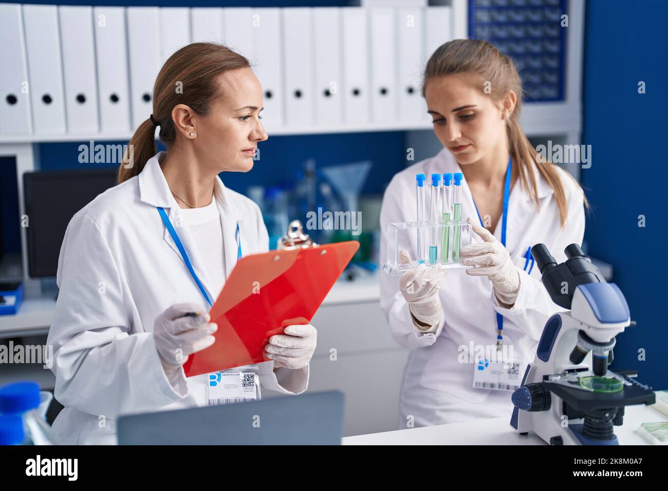 Two women scientists write on document holding test tubes at laboratory ...