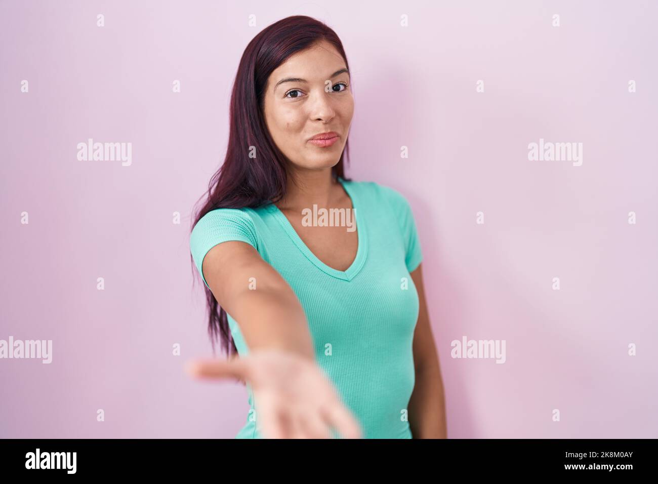 Young hispanic woman standing over pink background smiling cheerful ...