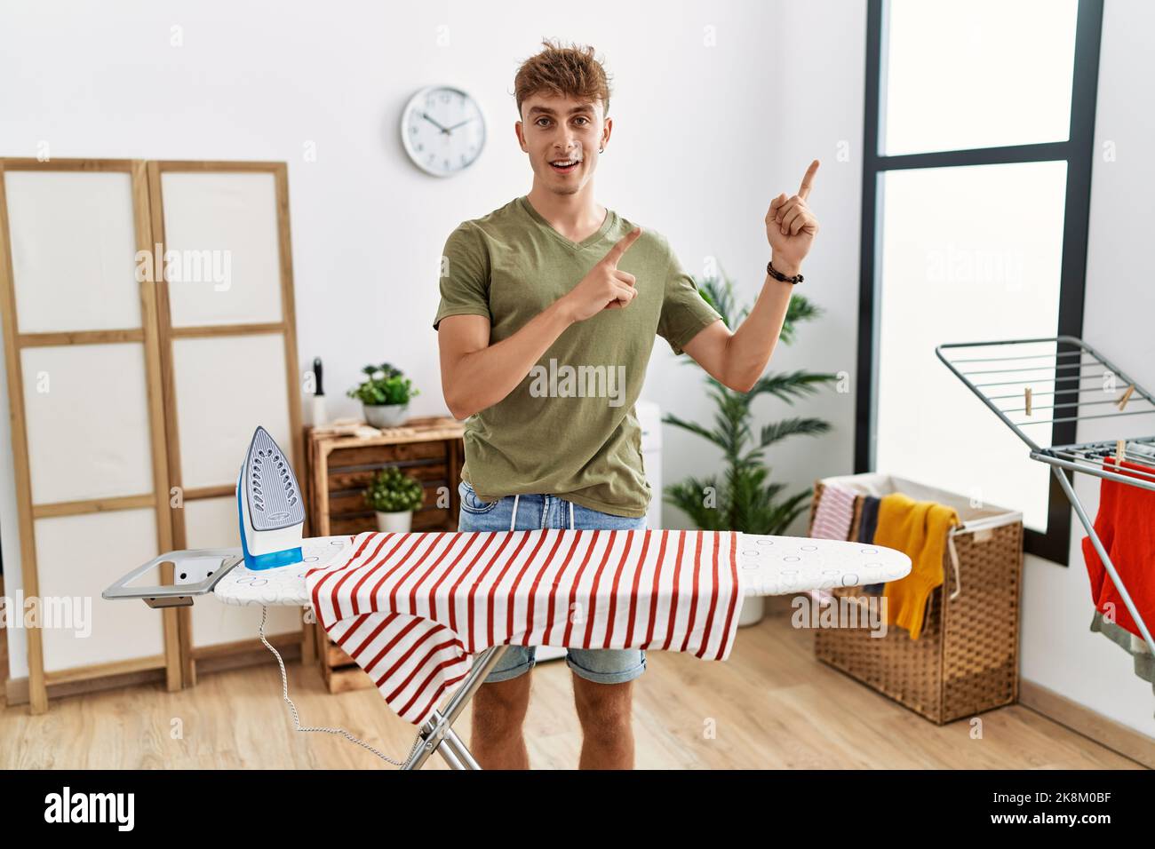 Young caucasian man ironing clothes at home smiling and looking at the ...