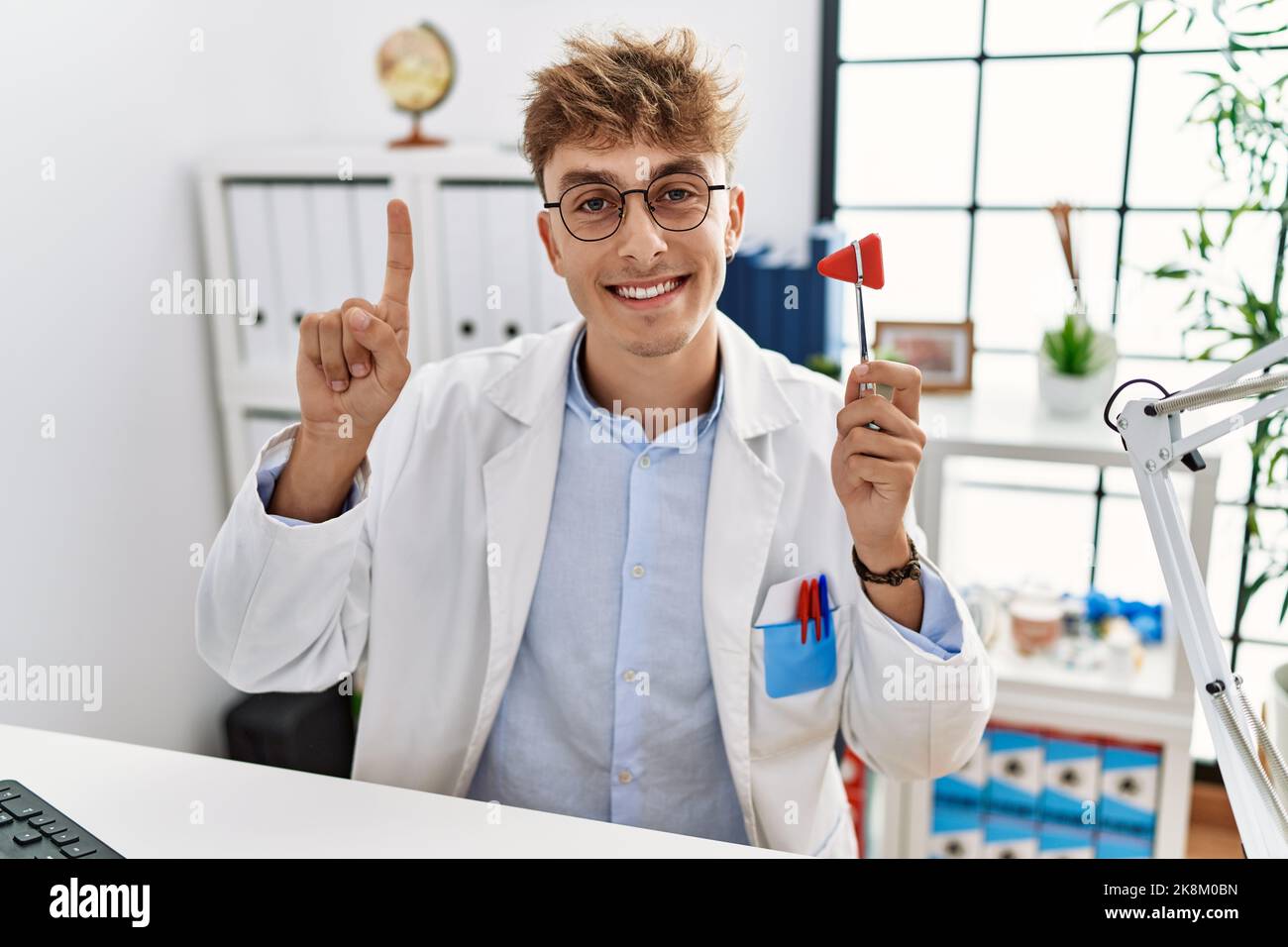 Young caucasian doctor man holding reflex hammer at the clinic smiling ...