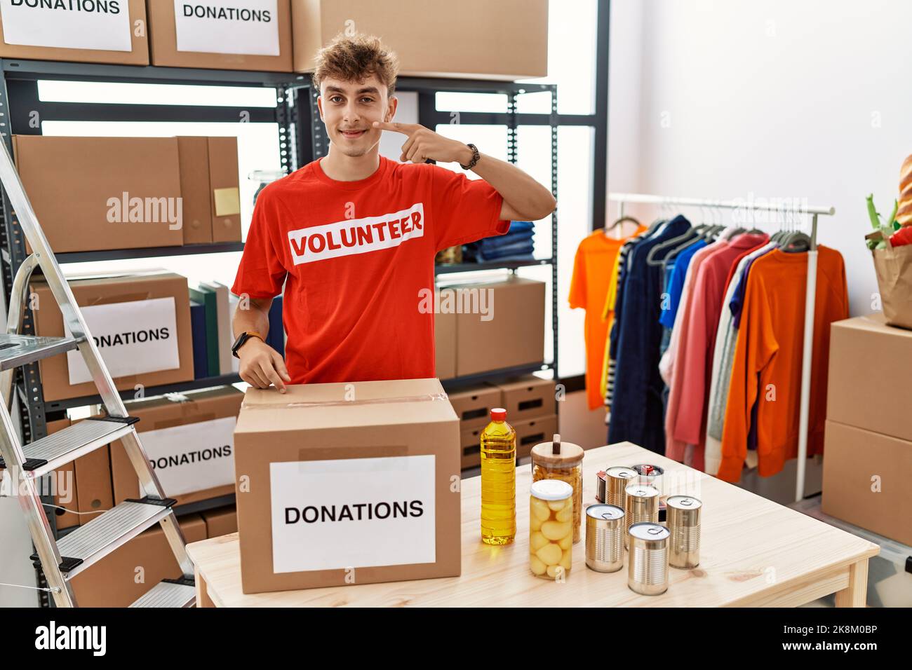 Young caucasian man volunteer holding donations box pointing with hand ...