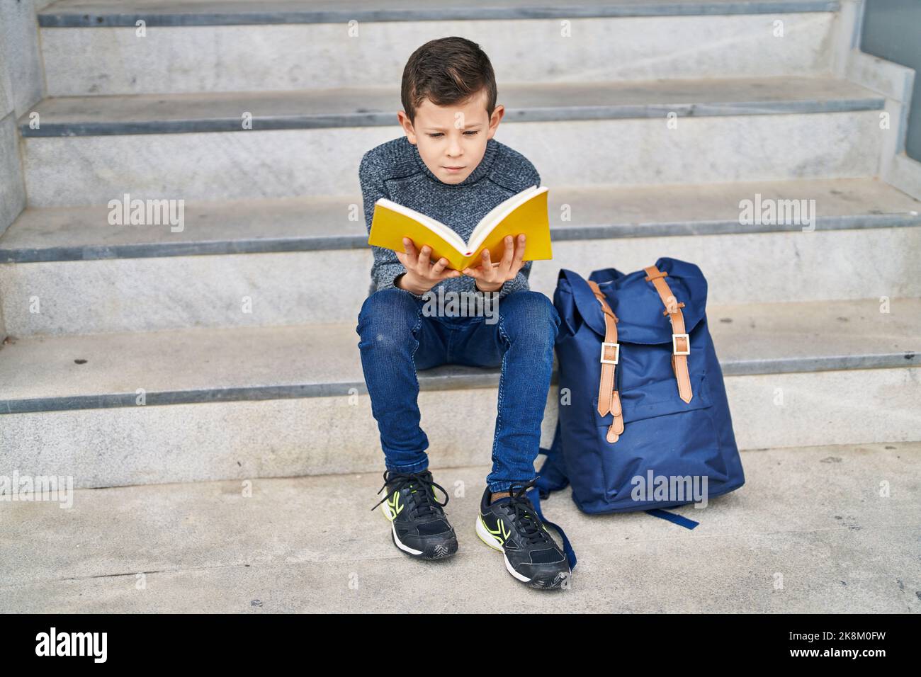 Blond child student reading book sitting on stairs at school Stock ...