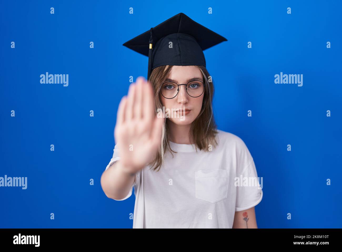 Blonde caucasian woman wearing graduation cap doing stop sing with palm ...