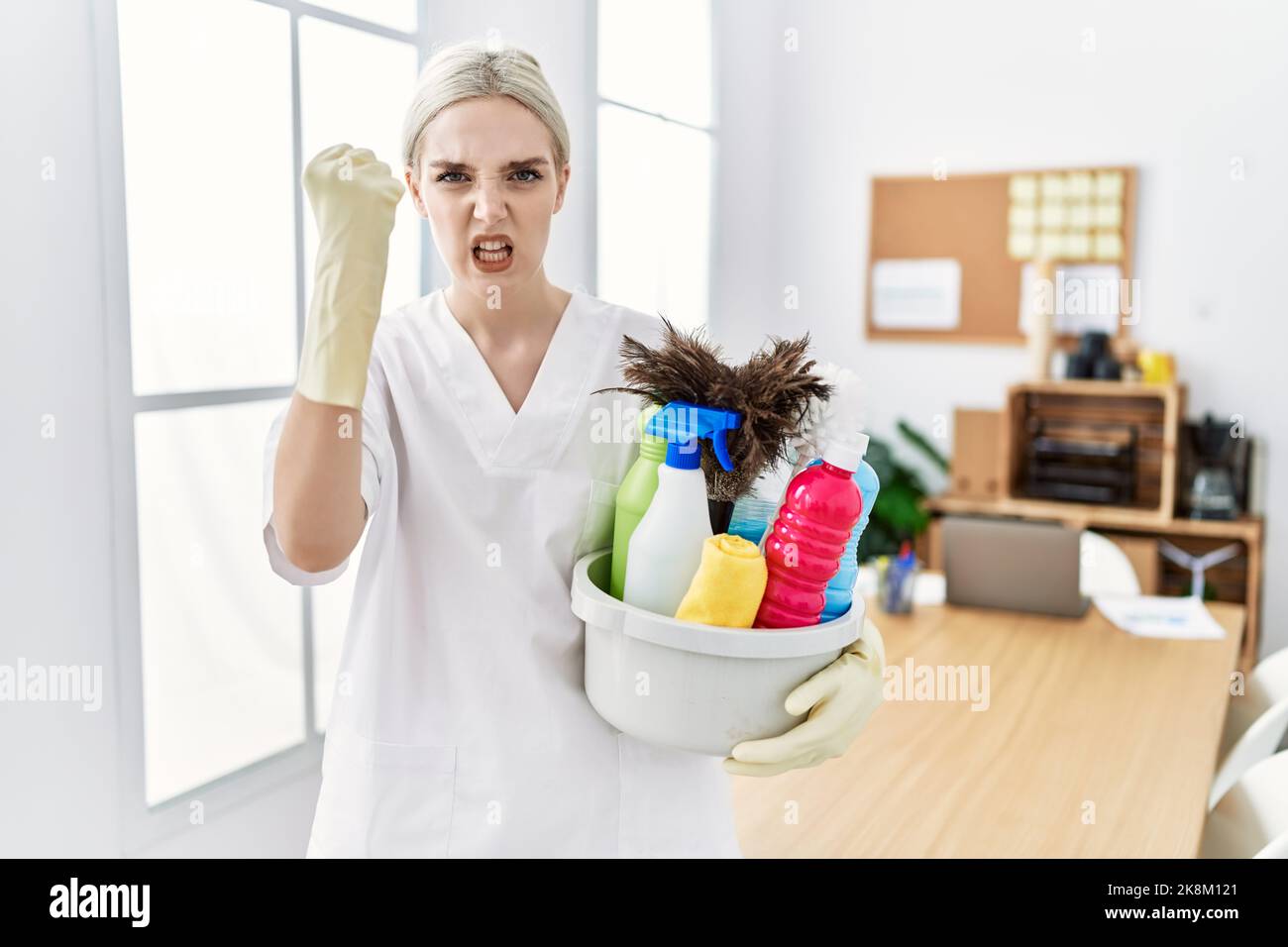 Young caucasian woman wearing cleaner uniform holding cleaning products ...