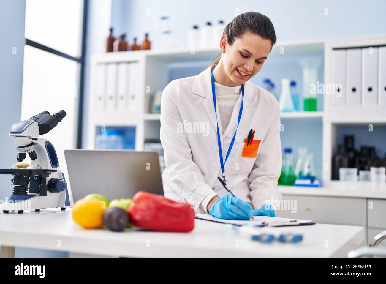 Young beautiful hispanic woman scientist using laptop writing on ...
