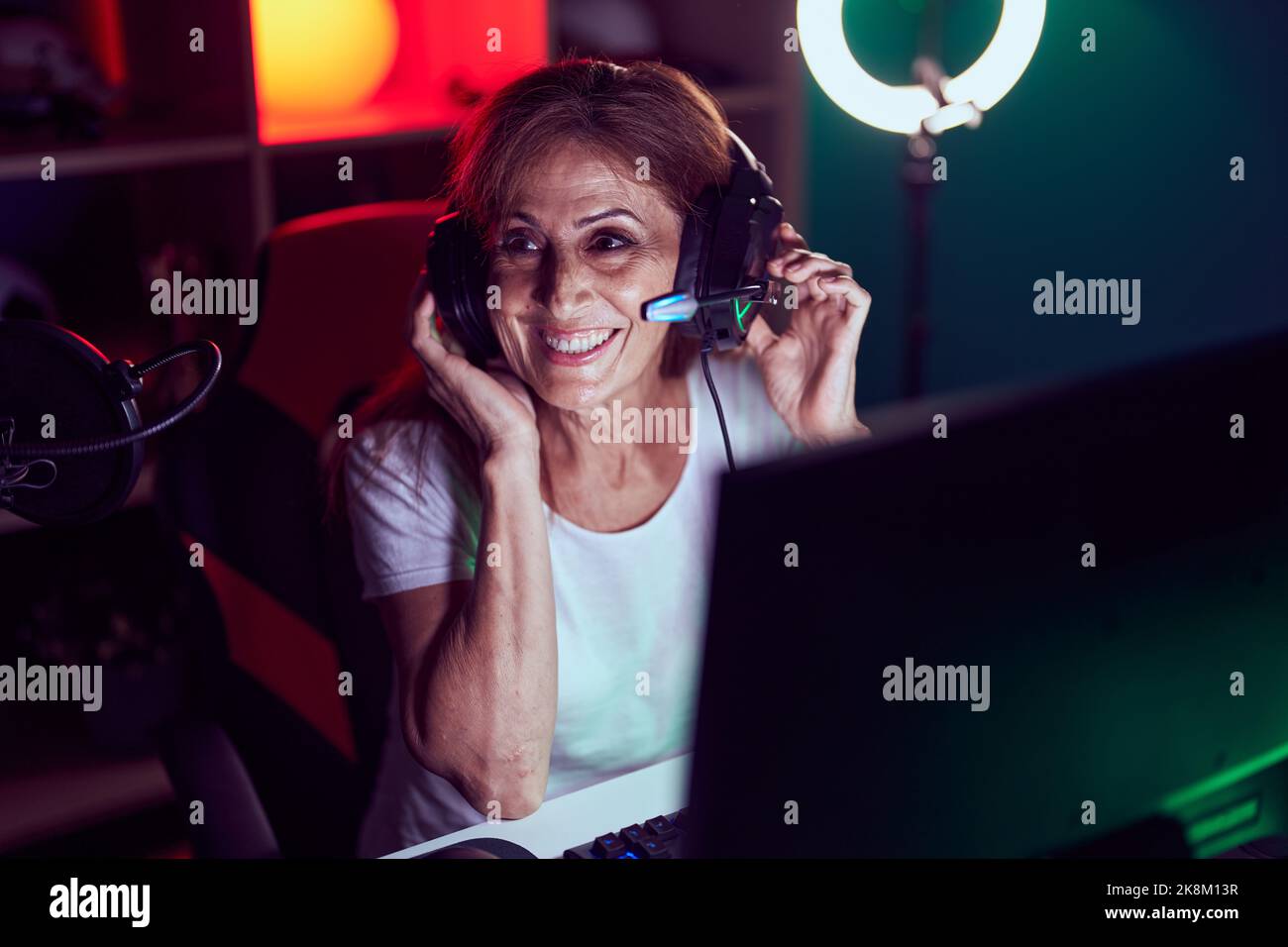 Middle age woman streamer playing video game using computer at gaming ...