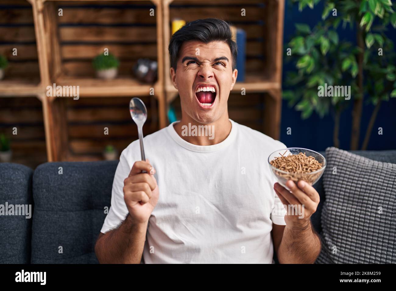 Hispanic man eating healthy whole grain cereals with spoon angry and ...