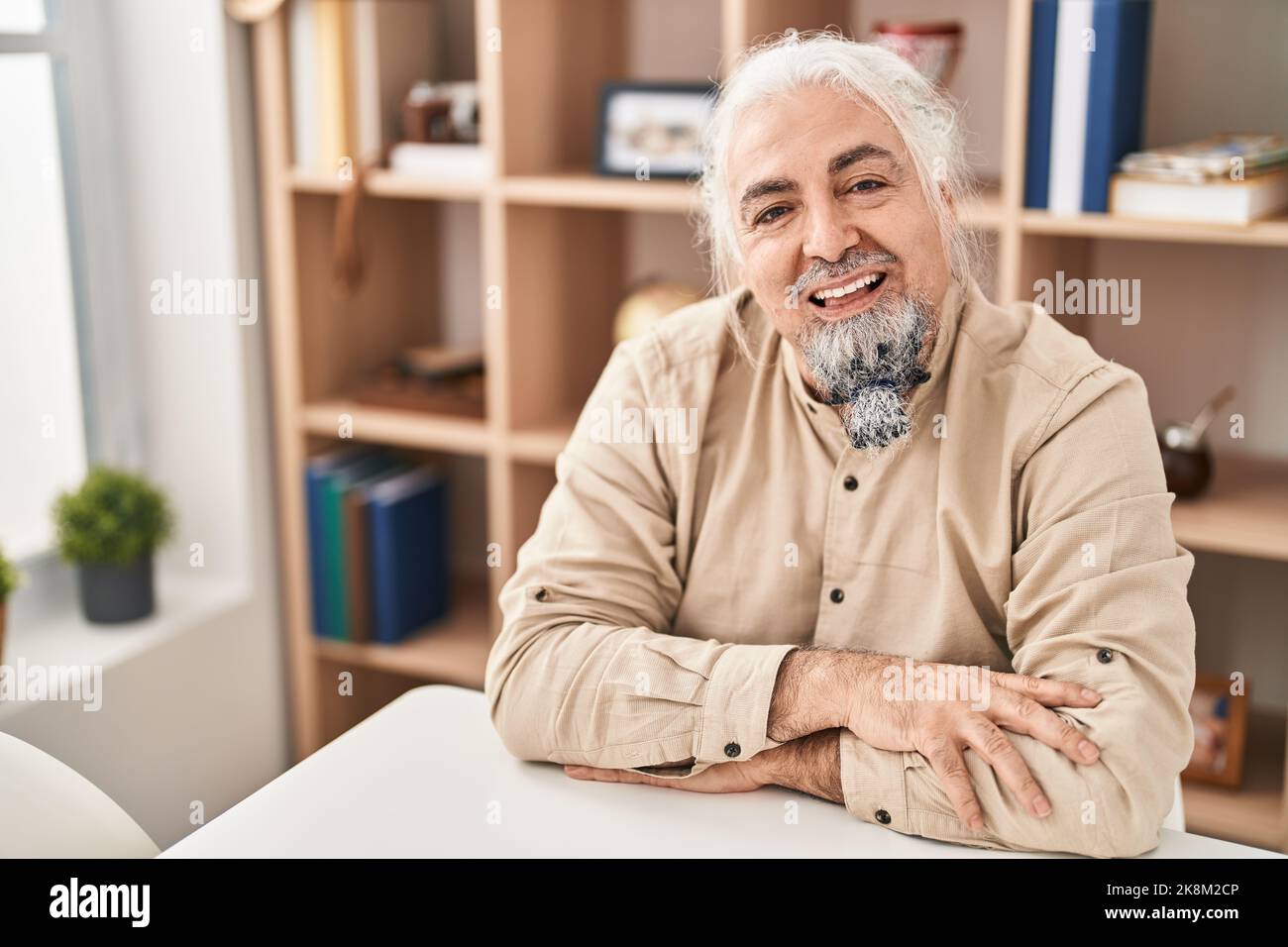 Middle age grey-haired man smiling confident sitting on table at home ...