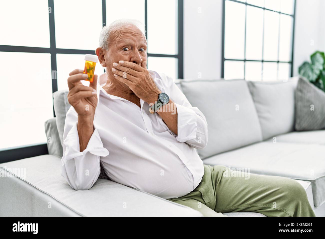 Senior man holding pills laughing and embarrassed giggle covering mouth ...