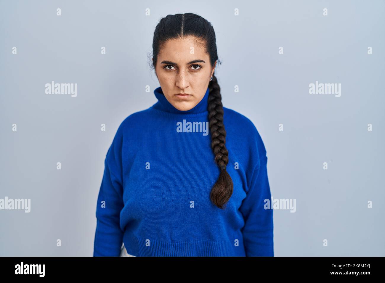 Young hispanic woman standing over isolated background skeptic and ...