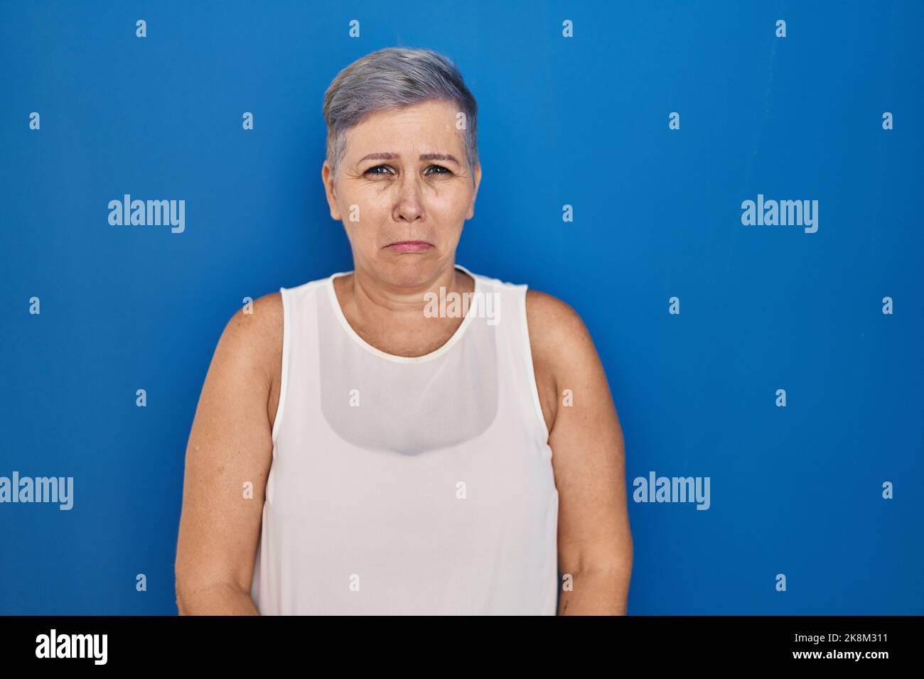 Middle age caucasian woman standing over blue background depressed and ...