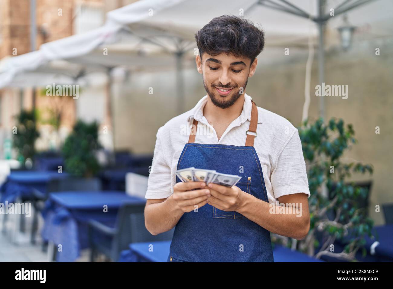 Young arab man waiter counting dollars working at restaurant Stock ...