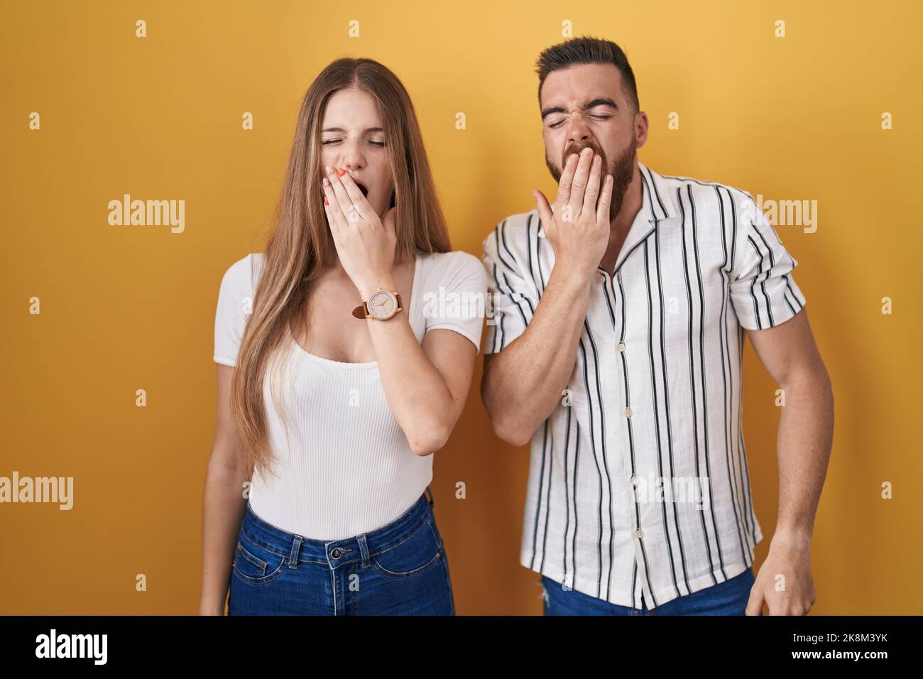Young couple standing over yellow background bored yawning tired ...