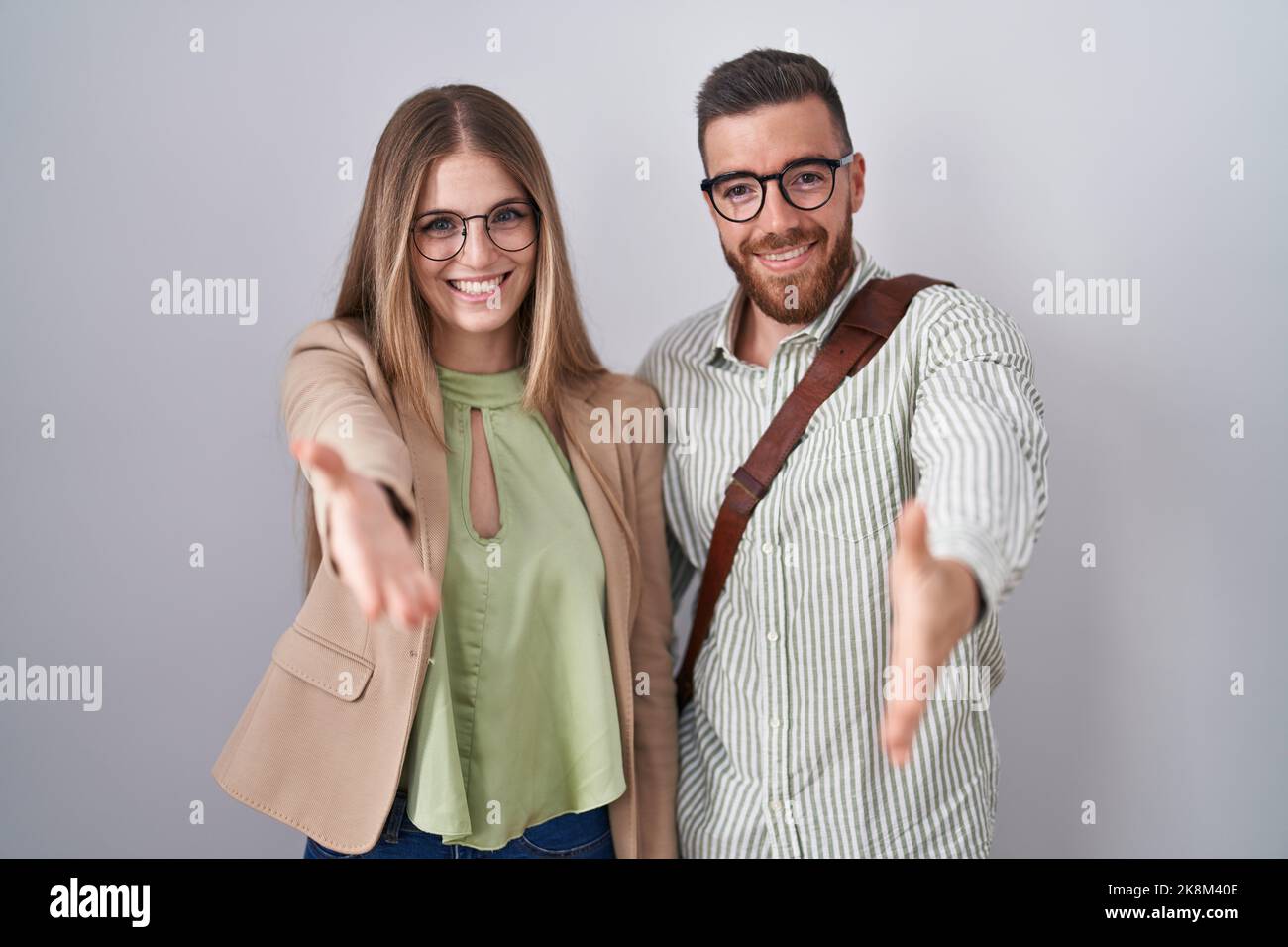 Young couple standing over white background smiling friendly offering ...