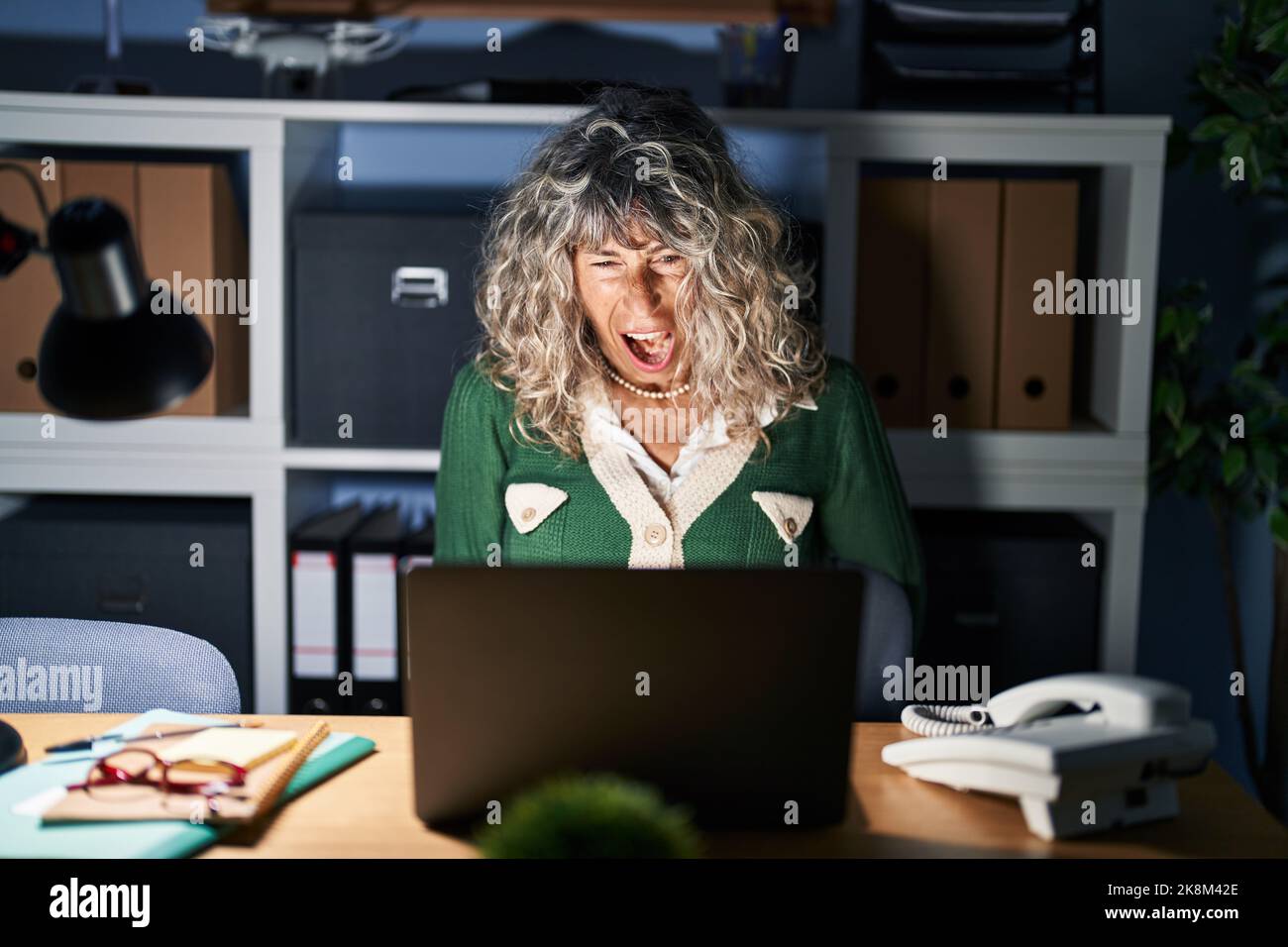 Middle age woman working at night using computer laptop angry and mad ...