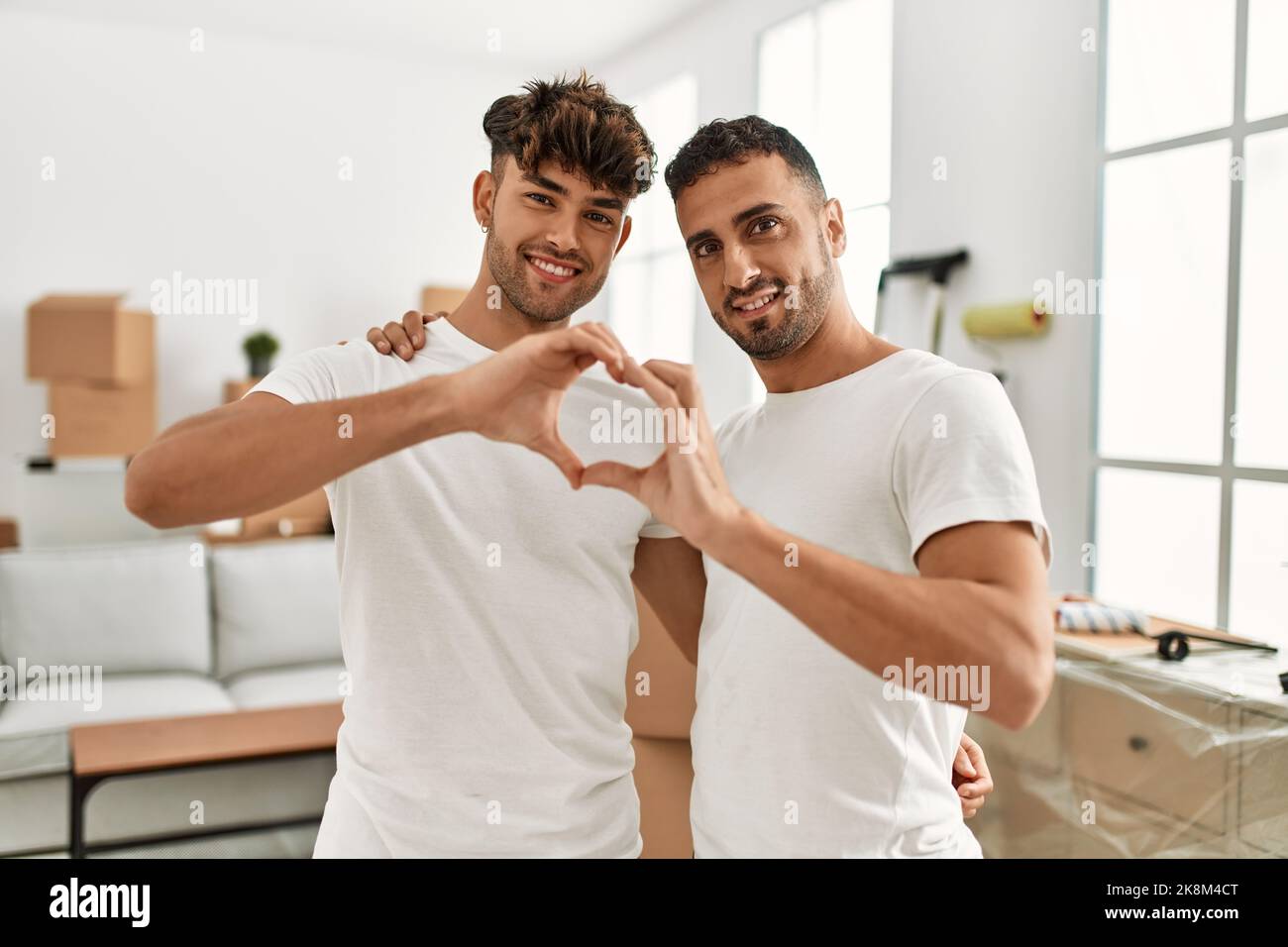 Two hispanic men couple hugging each other doing heart shape with hands ...