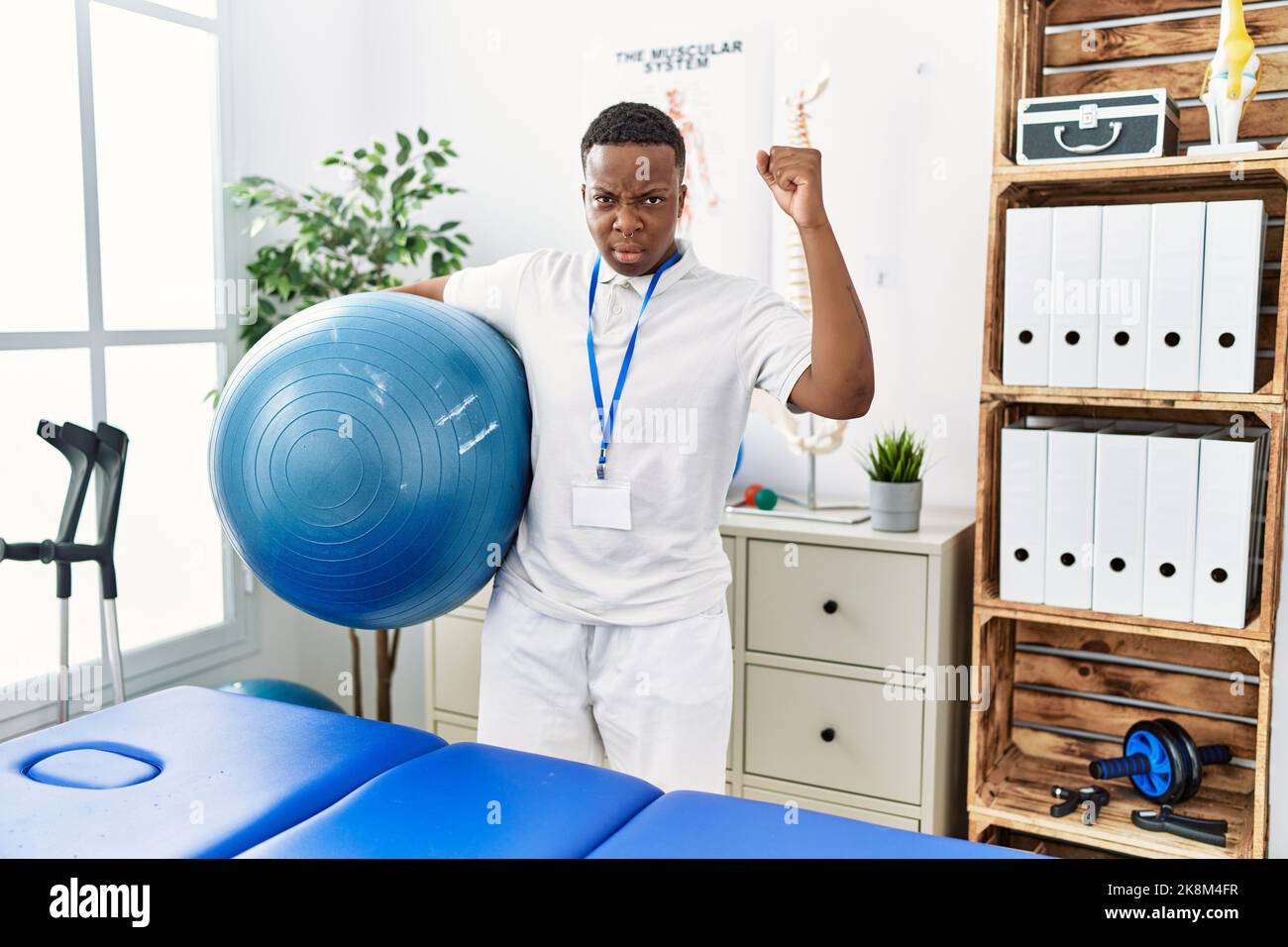 Young african physiotherapy man holding pilates ball at rehabilitation ...
