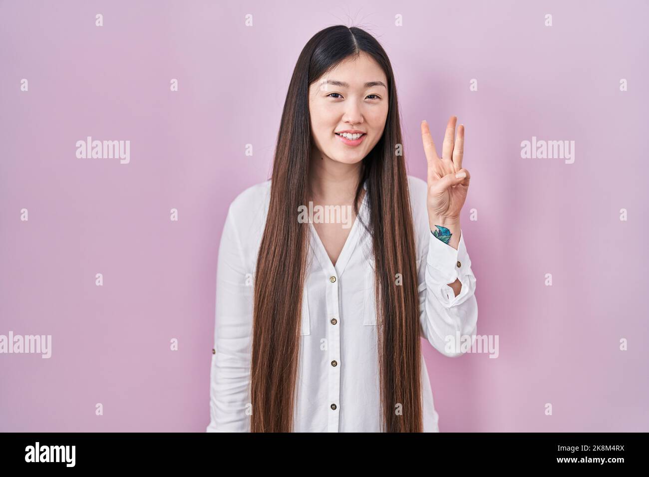 Chinese young woman standing over pink background showing and pointing ...