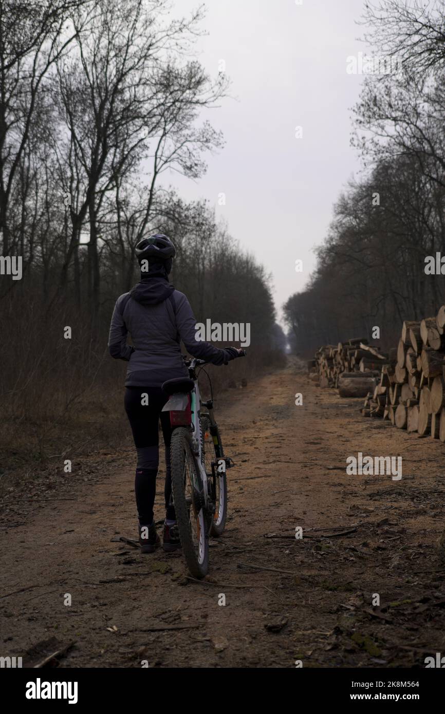 A vertical closeup shot of a female riding a bike in a forest path ...