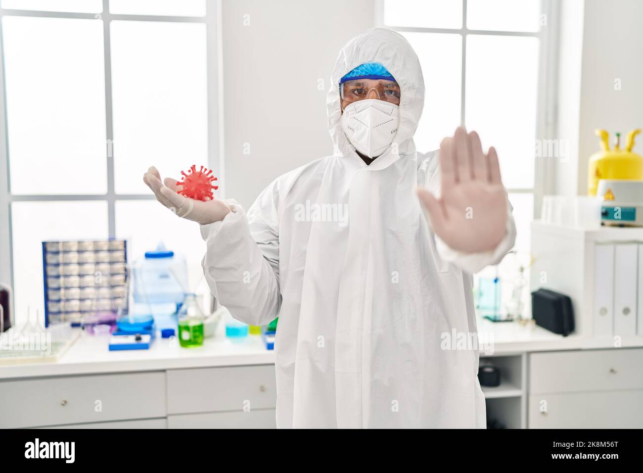 Hispanic young man working at scientist laboratory holding virus toy ...