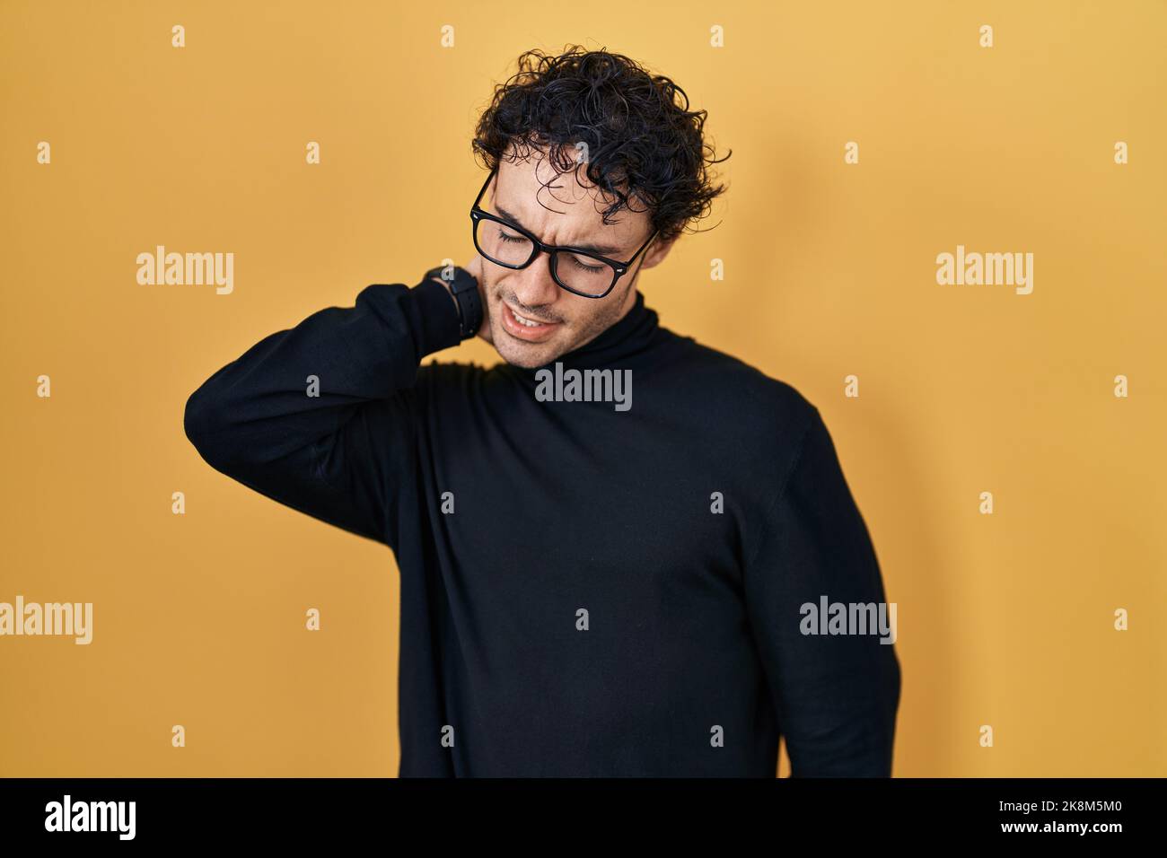 Hispanic man standing over yellow background suffering of neck ache ...
