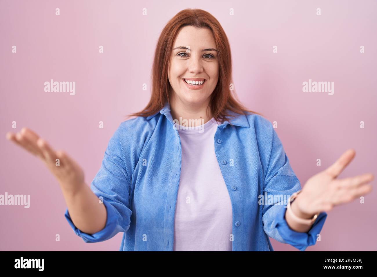 Young hispanic woman with red hair standing over pink background ...