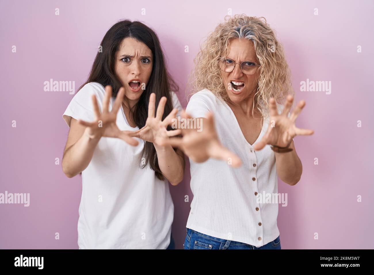 Mother and daughter standing together over pink background afraid and ...