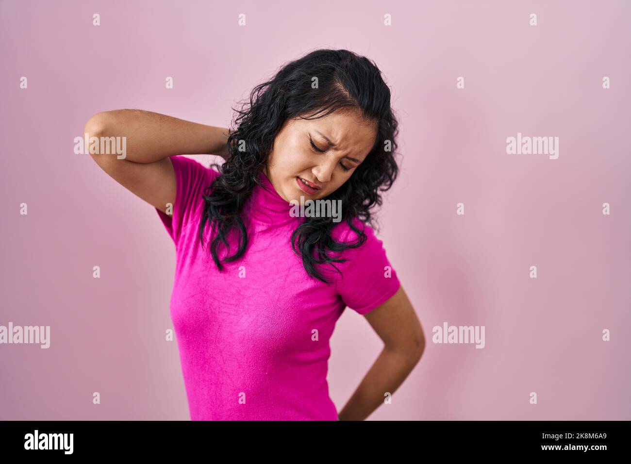 Young asian woman standing over pink background suffering of neck ache ...