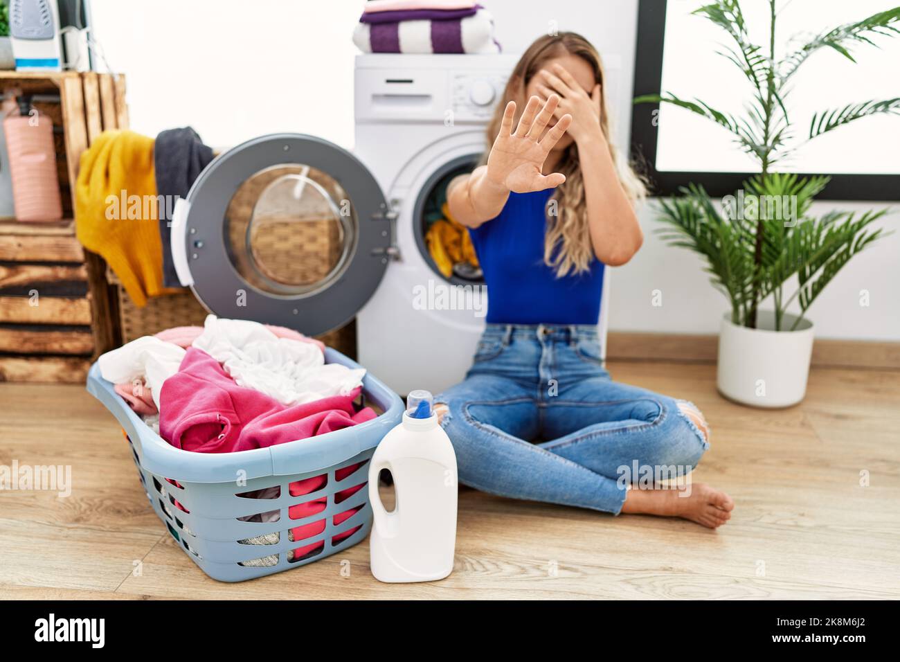 Young beautiful woman doing laundry sitting by wicker basket covering ...