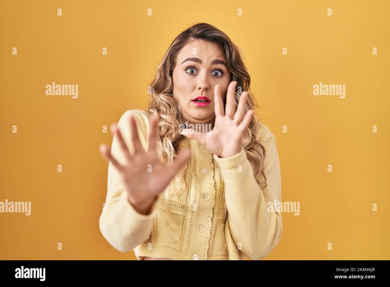Young caucasian woman standing over yellow background afraid and ...
