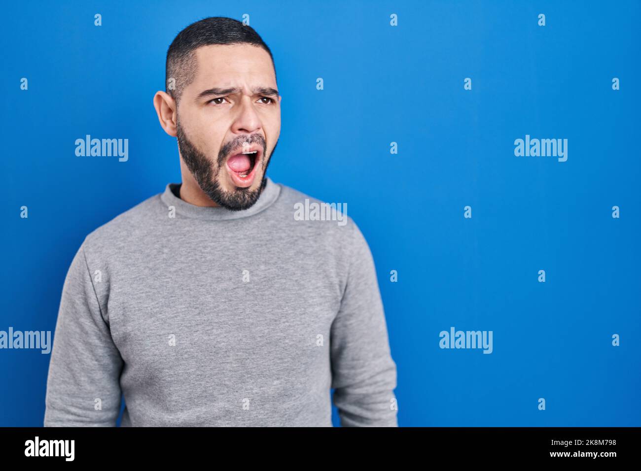 Hispanic man standing over blue background angry and mad screaming ...