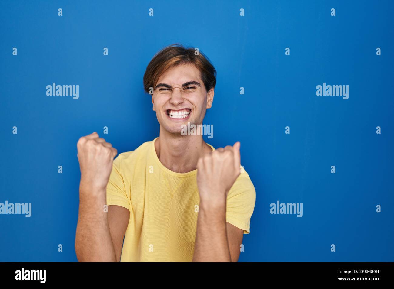 Young man standing over blue background very happy and excited doing ...
