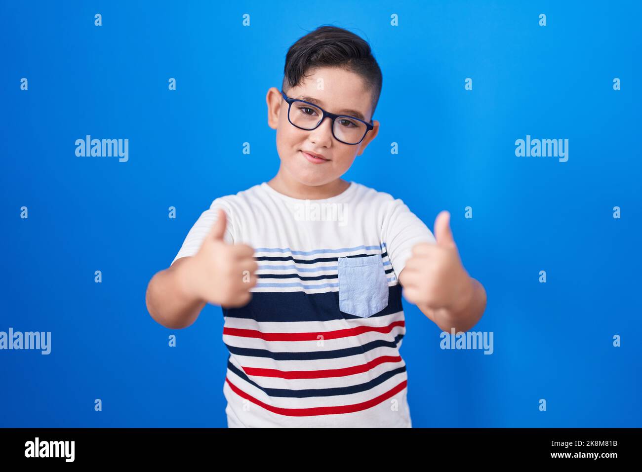 Young hispanic kid standing over blue background success sign doing ...