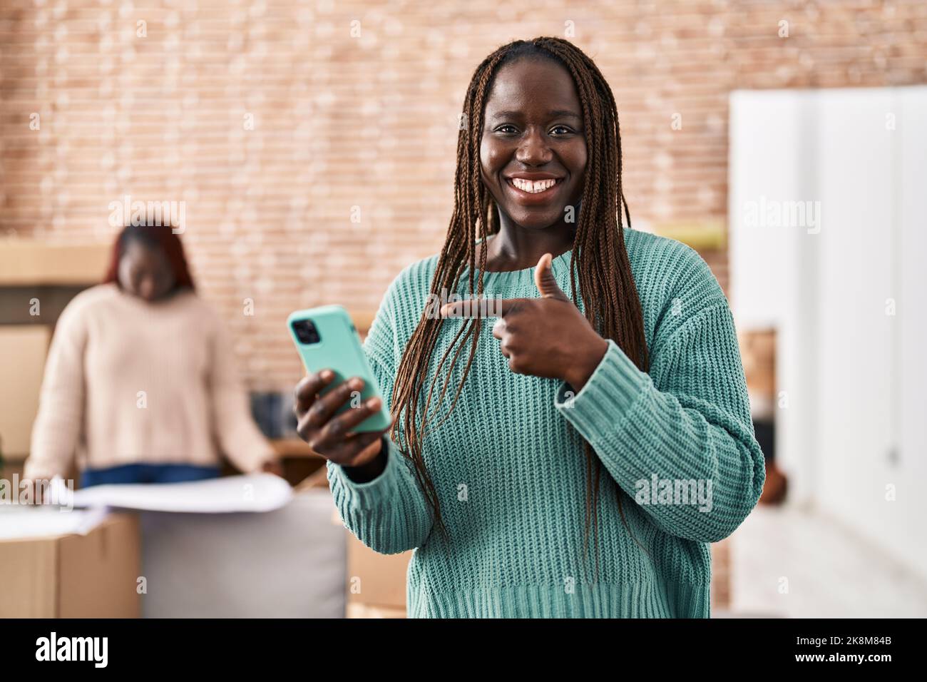 African woman using smartphone at new home smiling happy pointing with ...