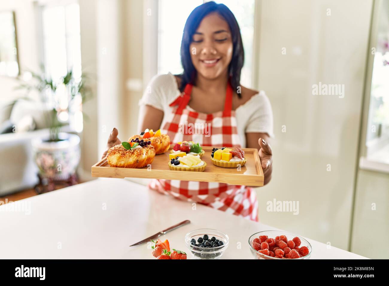 Hispanic brunette woman holding tray with pastries with fruits at the ...