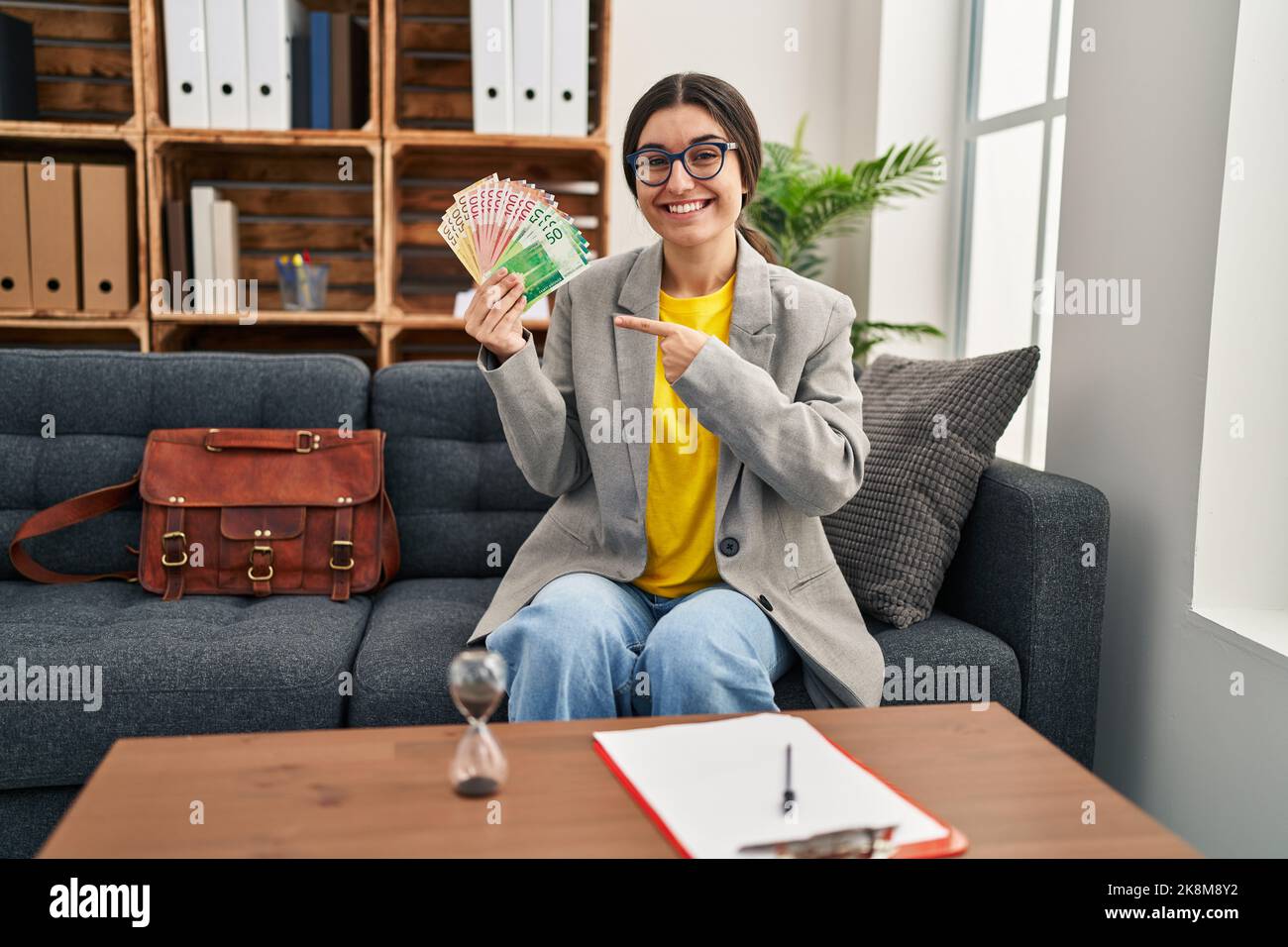 Young hispanic woman working at consultation office holding money ...