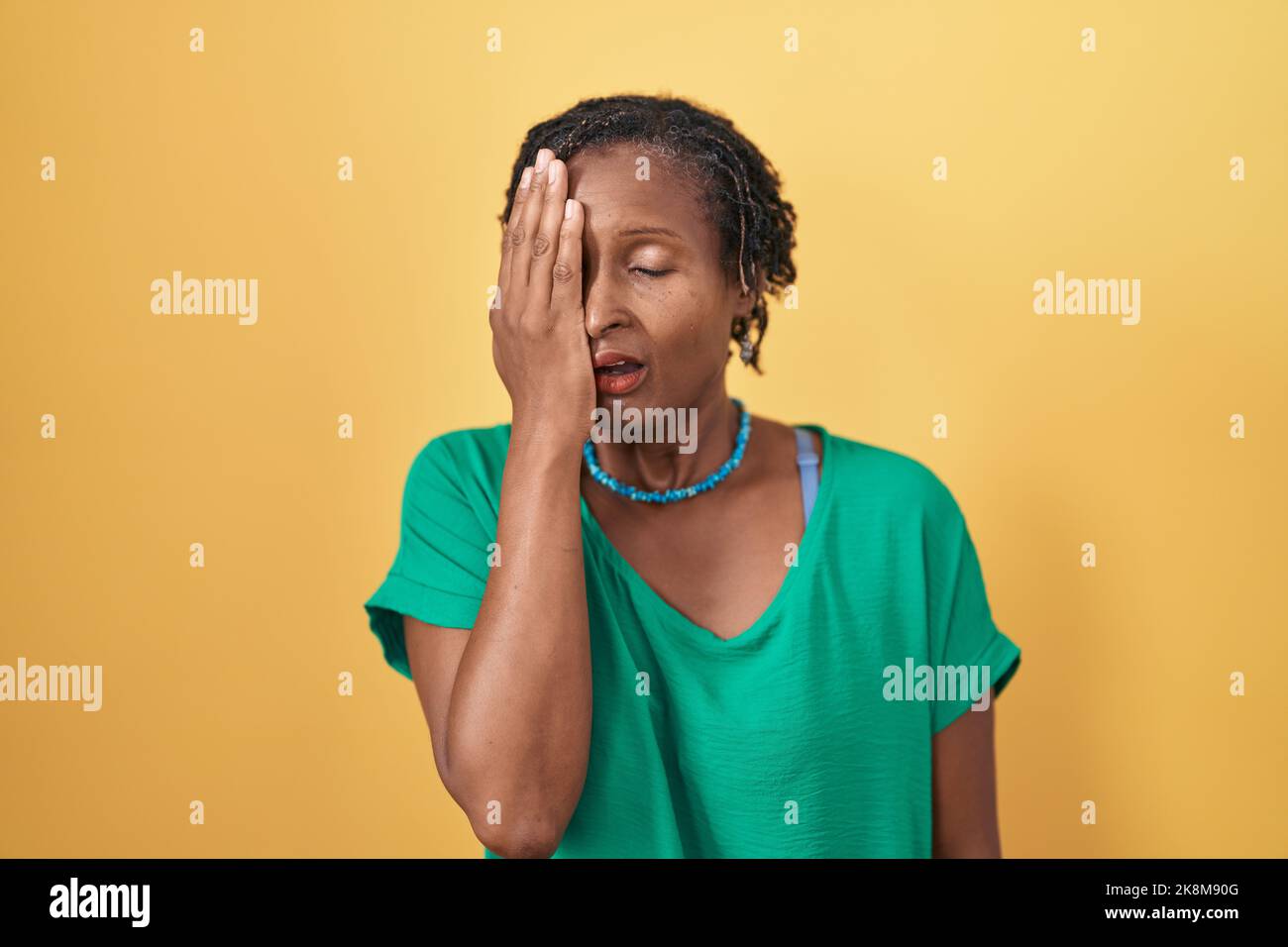 African woman with dreadlocks standing over yellow background yawning ...