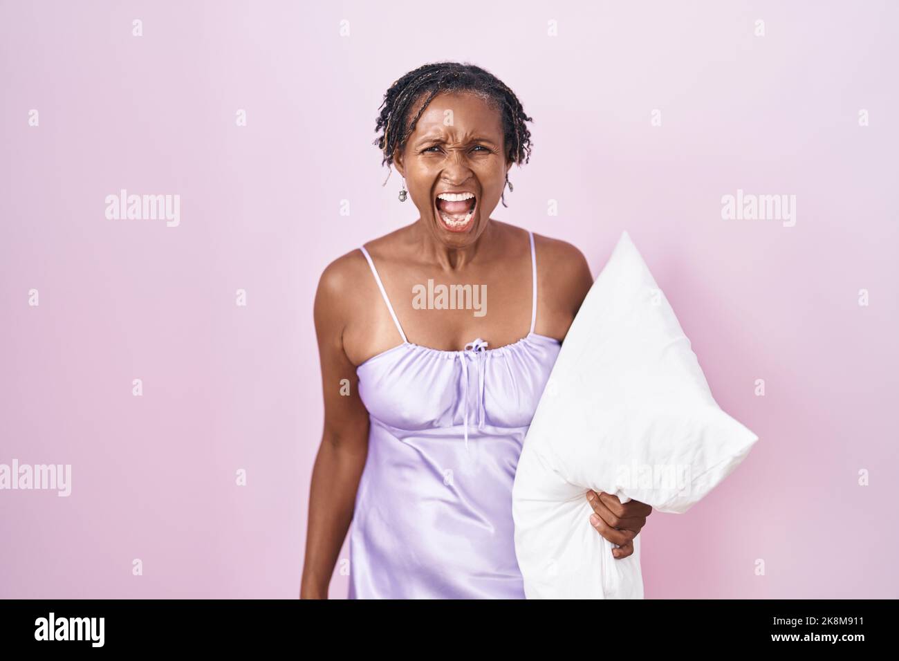 African woman with dreadlocks wearing pajama hugging pillow angry and ...