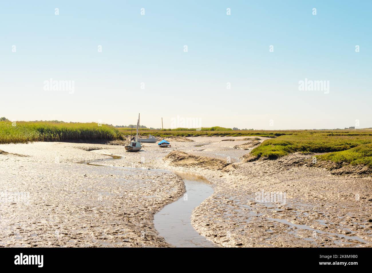 A narrow river surrounded by wet soil and greenery and two boats in the ...