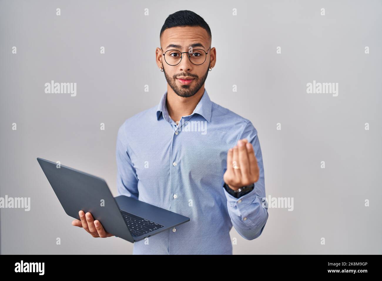 Young hispanic man working using computer laptop doing money gesture ...