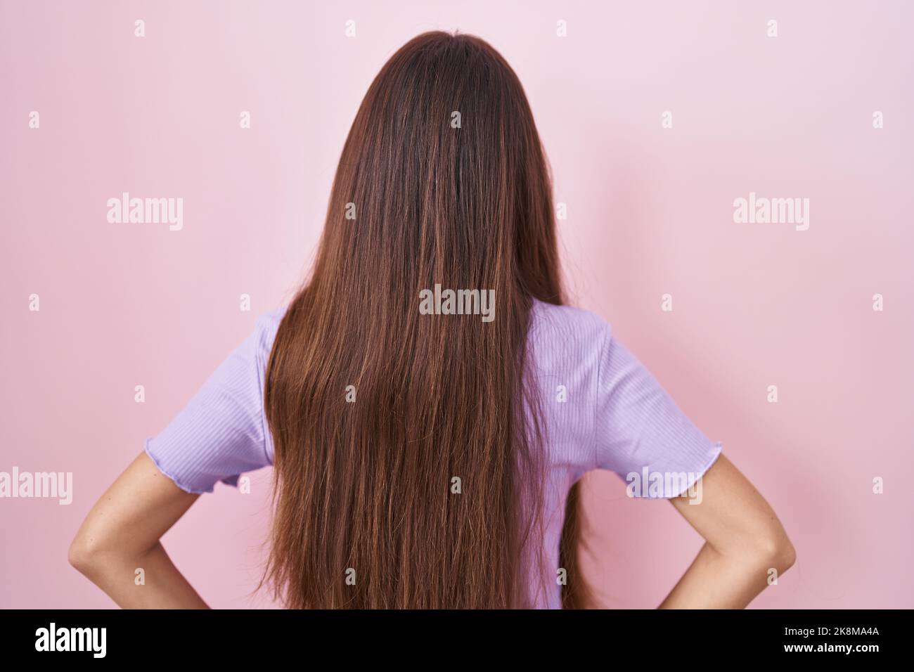 Young hispanic woman with long hair standing over pink background ...