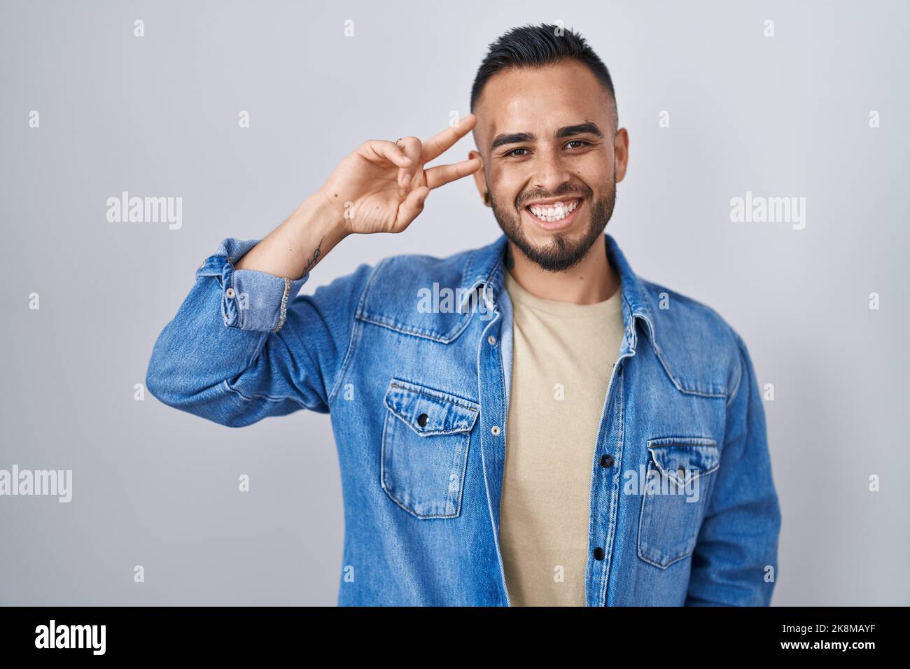 Young hispanic man standing over isolated background doing peace symbol ...