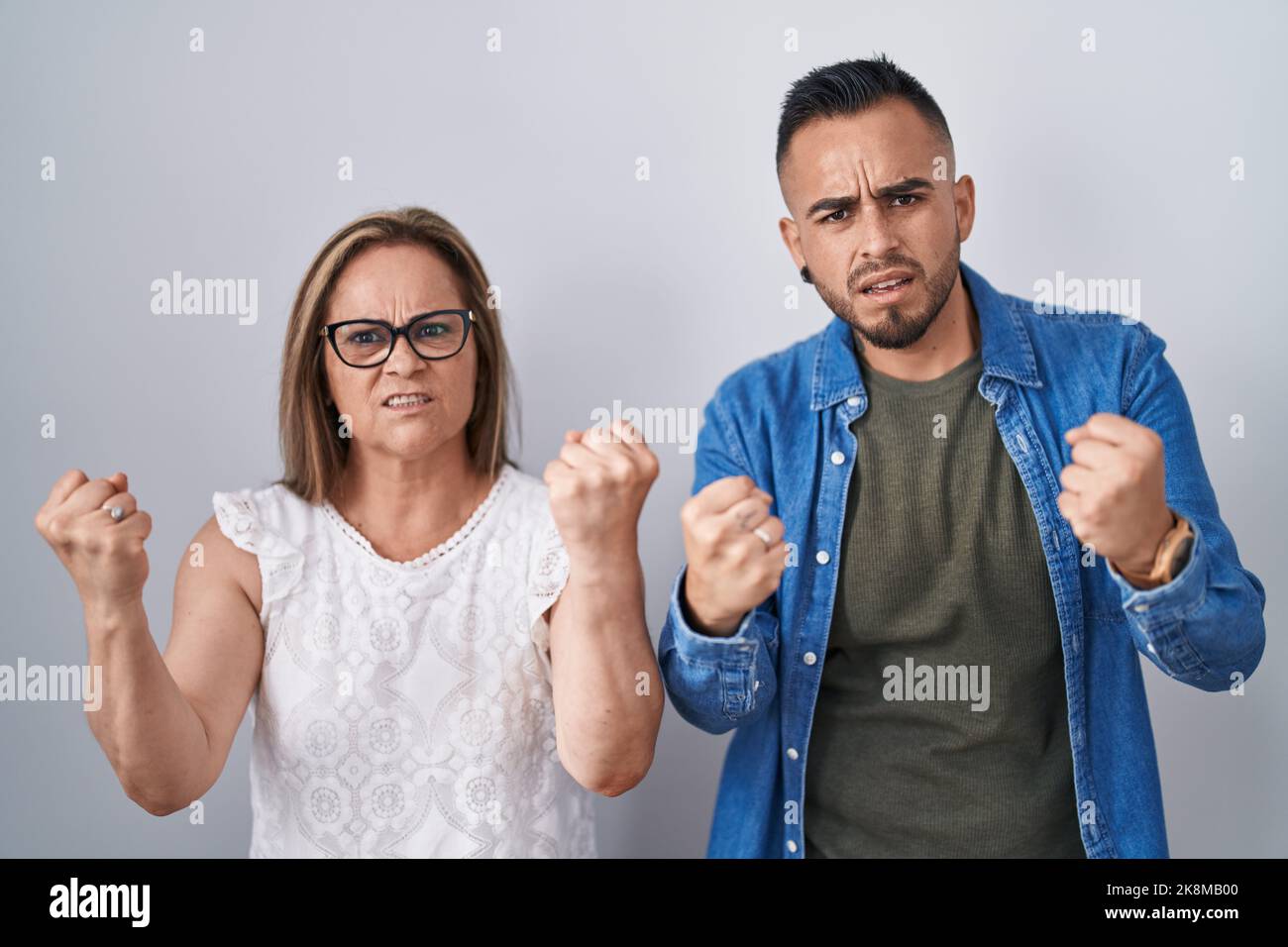 Hispanic mother and son standing together angry and mad raising fists ...