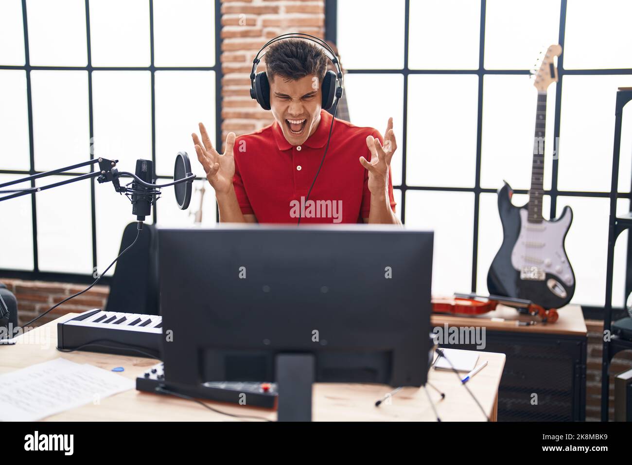 Young hispanic man playing piano keyboard at music studio crazy and mad ...