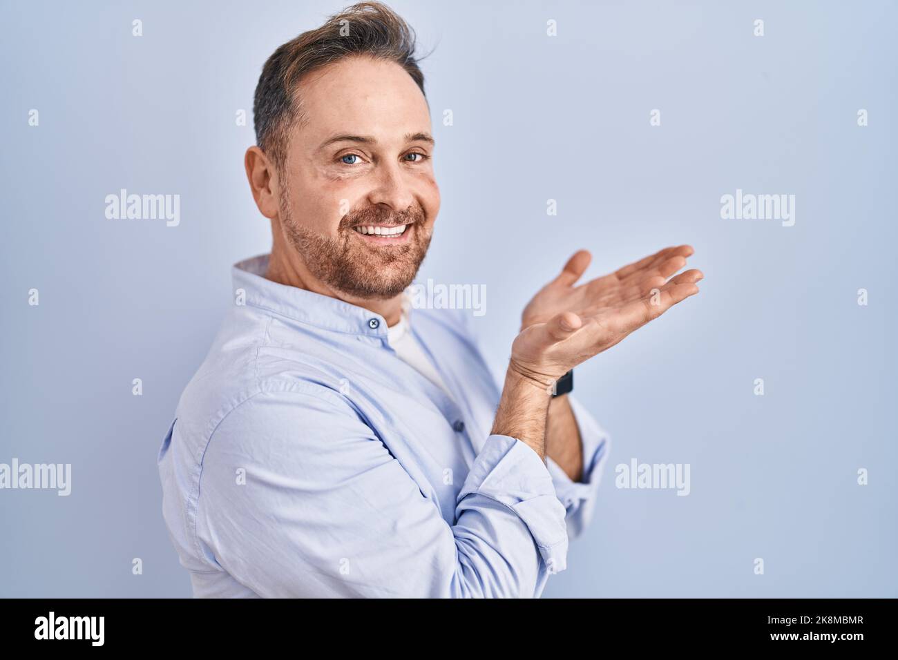 Middle age caucasian man standing over blue background pointing aside ...