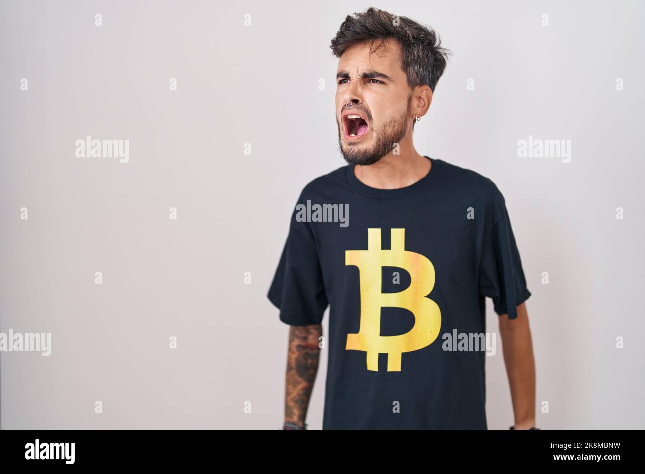 Young hispanic man with tattoos wearing bitcoin t shirt angry and mad ...