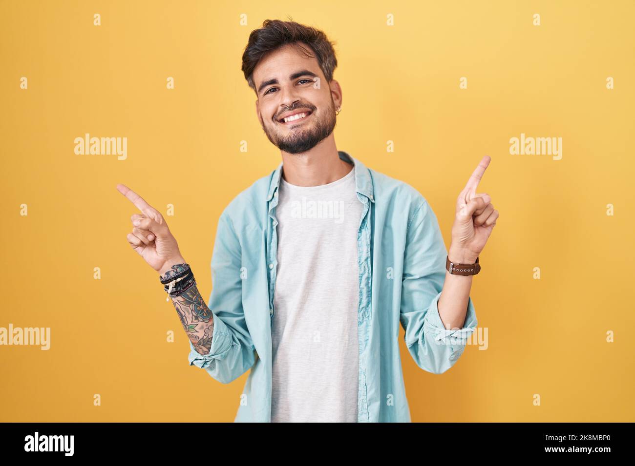 Young hispanic man with tattoos standing over yellow background smiling ...