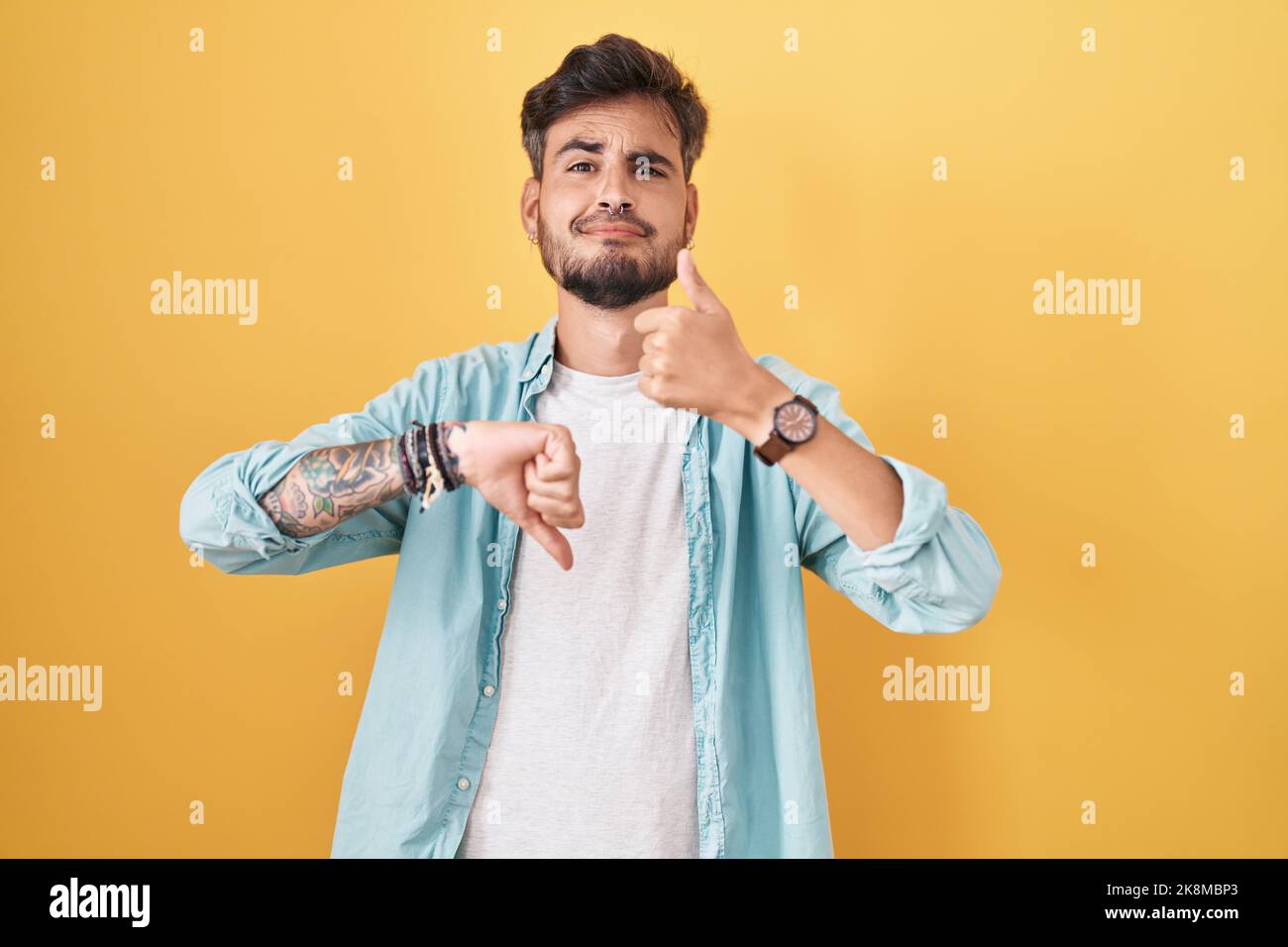 Young hispanic man with tattoos standing over yellow background doing ...