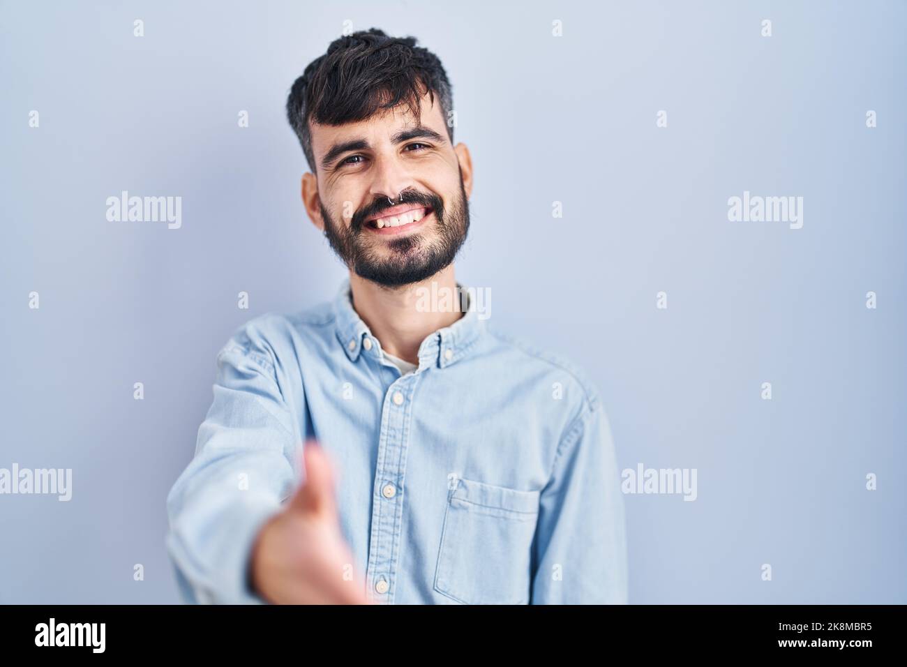 Young hispanic man with beard standing over blue background smiling ...