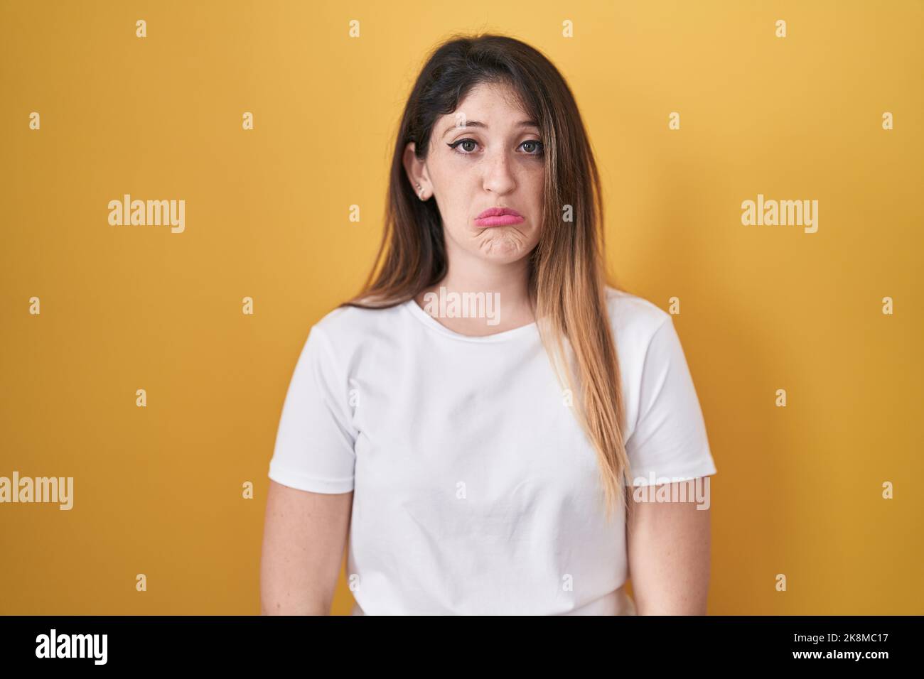 Young brunette woman standing over yellow background depressed and ...